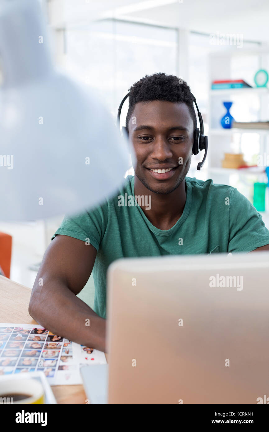 Male executive in headset working over computer at his desk in office ...