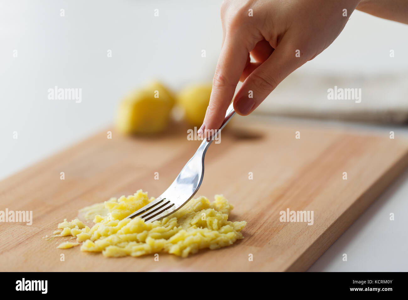 hand with fork making mashed potato on board Stock Photo - Alamy