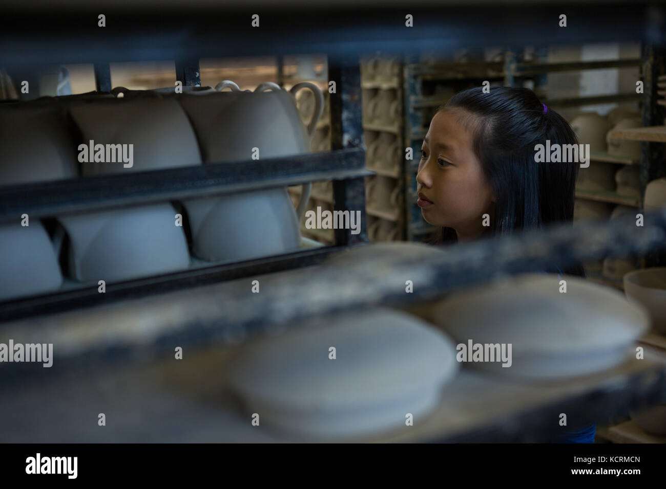 Girl arranging cups in shelf at pottery workshop Stock Photo - Alamy