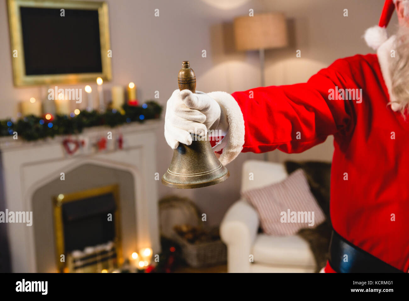 Mid-section of santa claus ringing a bell at home during christmas time ...