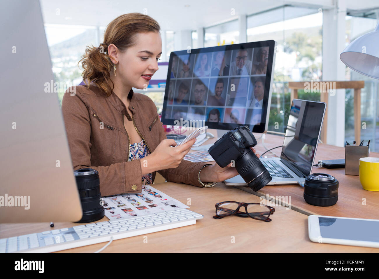 Smiling female executive using mobile phone while looking at digital ...