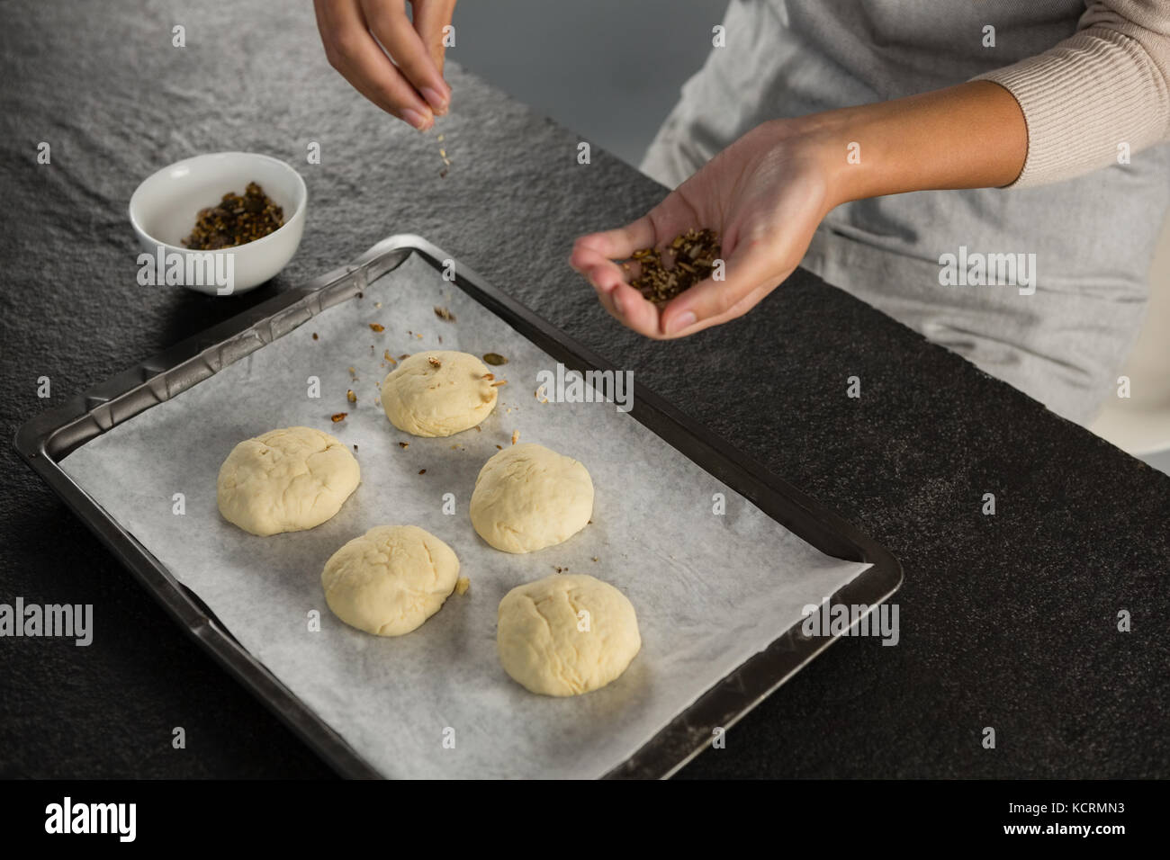 Woman adding dry fruits over unbaked cookie dough in a baking tray ...