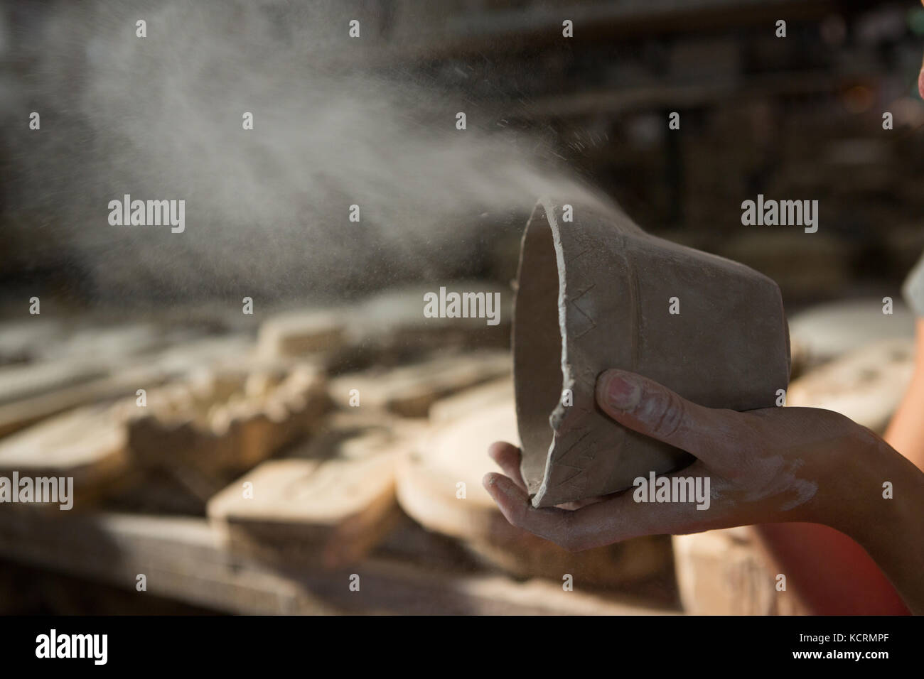 Female potter blowing dust from mud in pottery workshop Stock Photo - Alamy