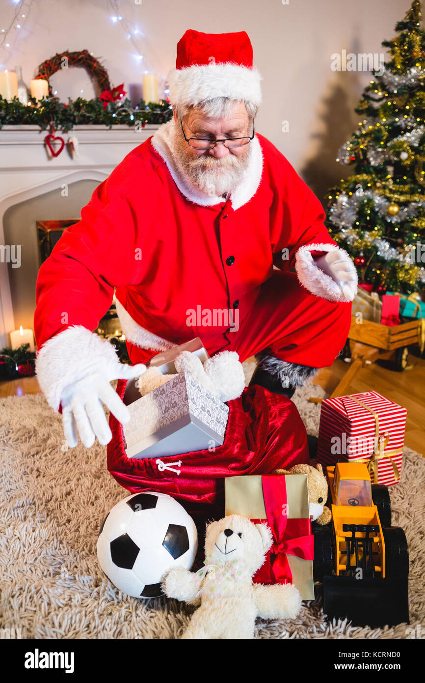 Santa claus placing gift box into gift sack at home during christmas ...