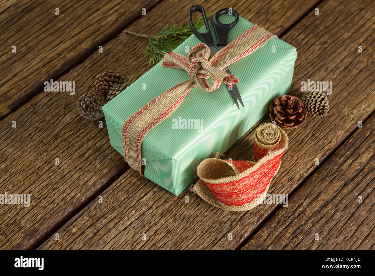 Scissors, pine cones, leaves and ribbon with wrapped gift box on wooden ...