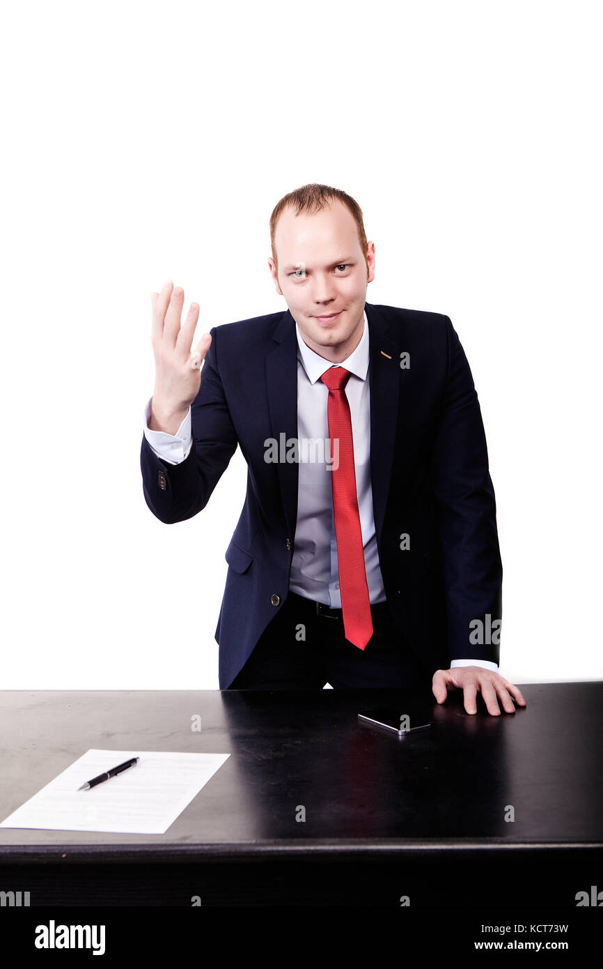 A man in a suit is standing at a table with a raised hand, on the table ...