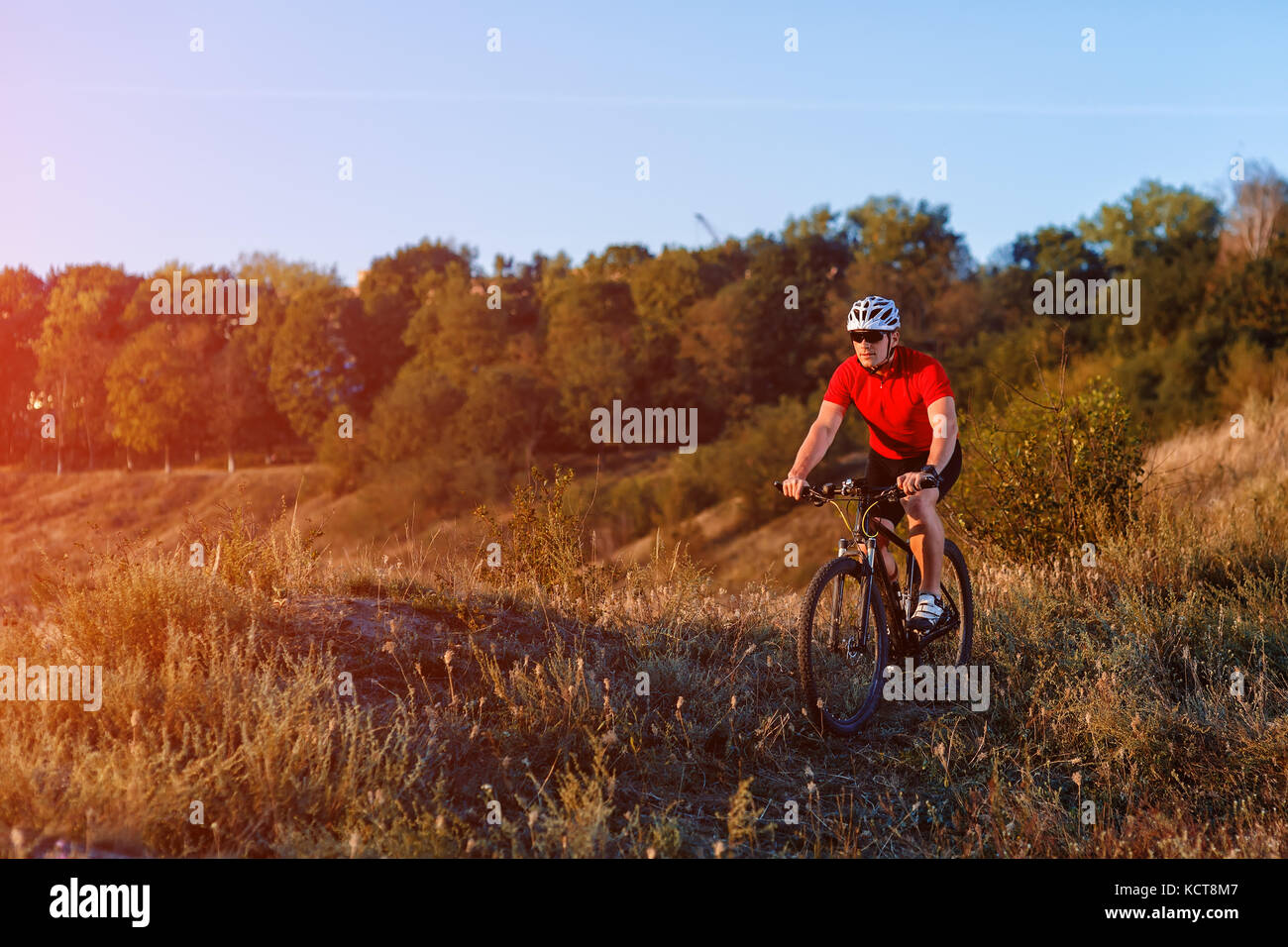 young bright man on mountain bike riding in autumn landscape against ...