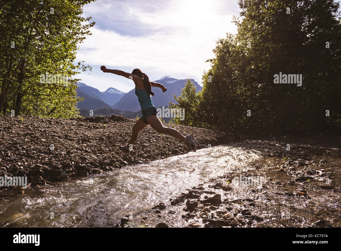 Jogger jumping through flowing water on sunny day Stock Photo - Alamy