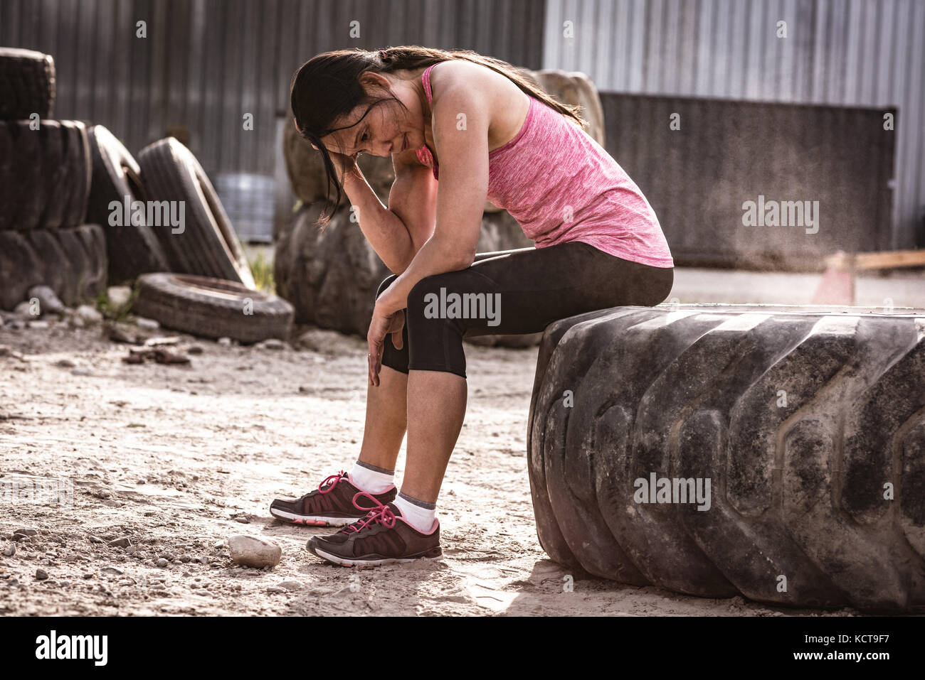 Tense fit woman sitting on tyre on a sunny day Stock Photo - Alamy