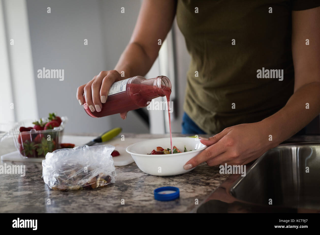 Mid section of woman pouring syrup in chopped strawberry at home Stock ...