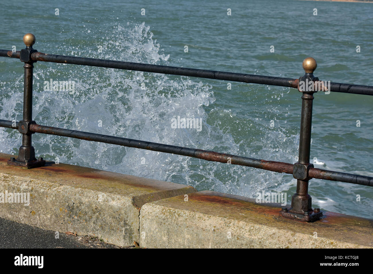the sea crashing against some wrought iron railings on the seafront on ...