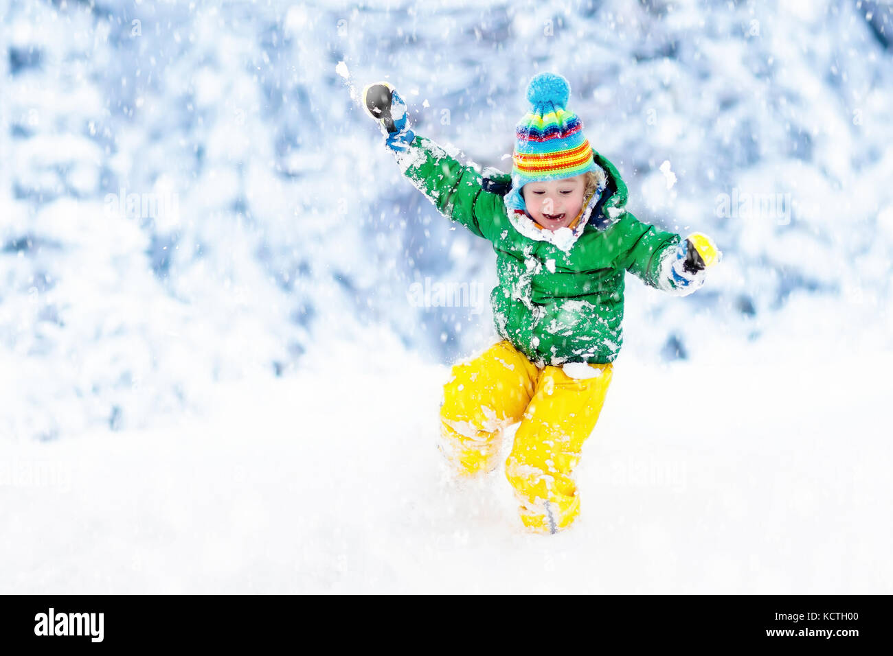 Child playing with snow in winter. Little boy in colorful jacket and ...