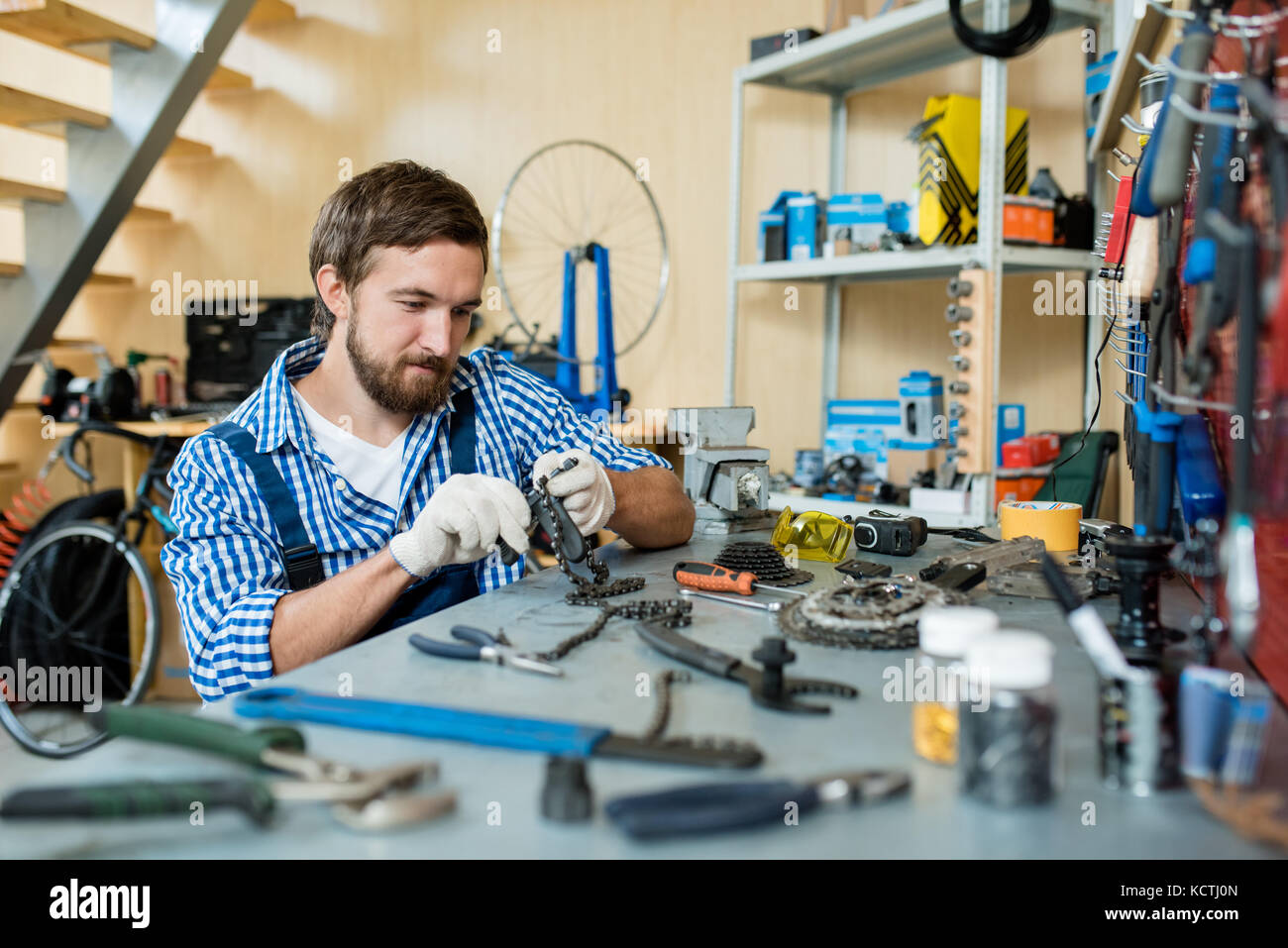 Modern mechanic repairing chain from bicycle wheel by his workplace ...