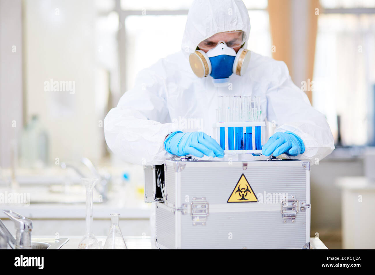 Concentrated scientist wearing hazmat suit examining test tubes while ...