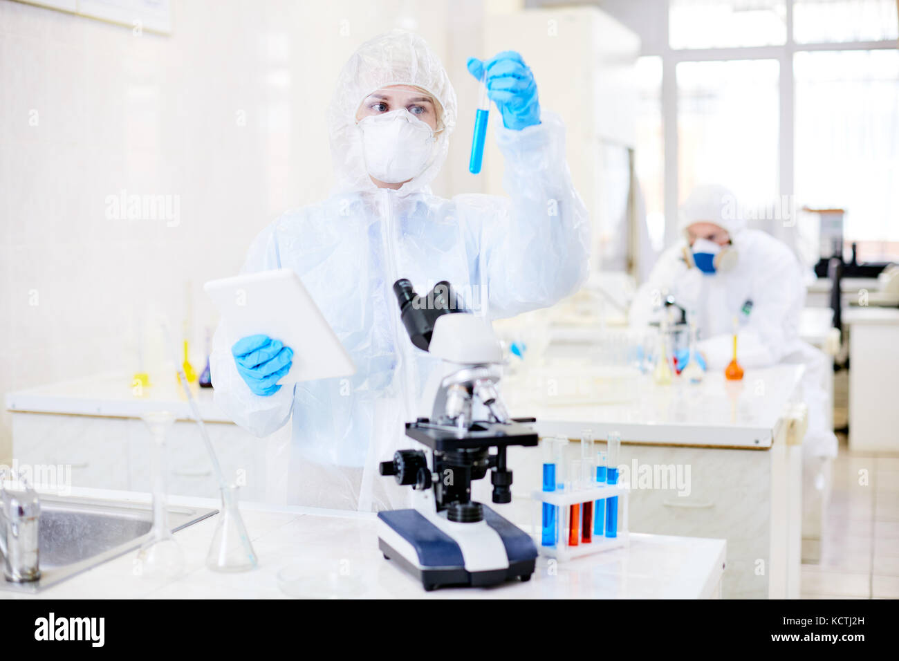 Gifted young microbiologist wearing filtering mask and coverall using ...