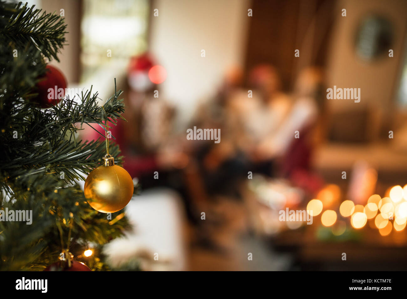 Close up of decorated christmas tree in living room with family sitting ...