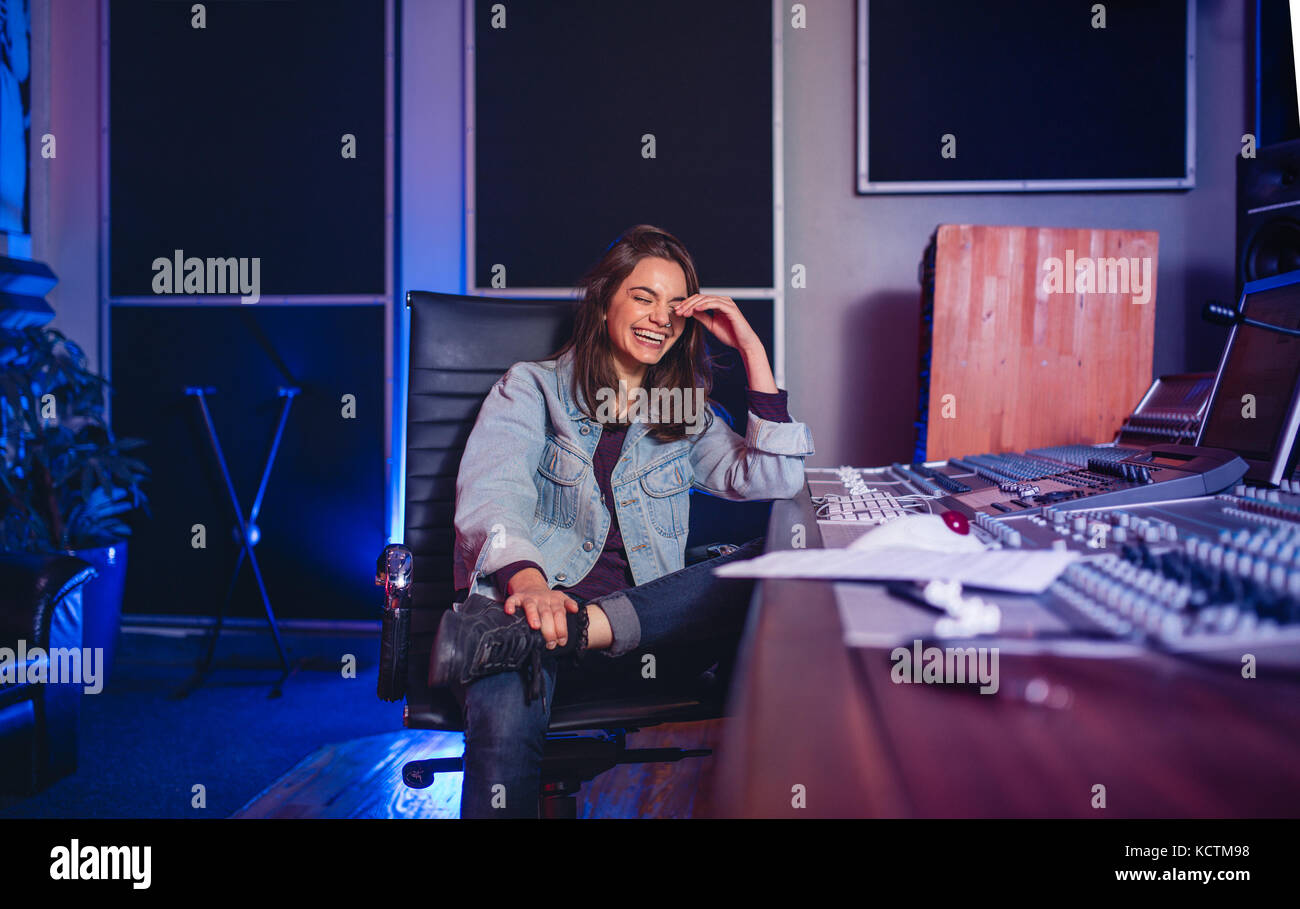 Female engineer sitting at mixing desk in recording studio. Smiling ...