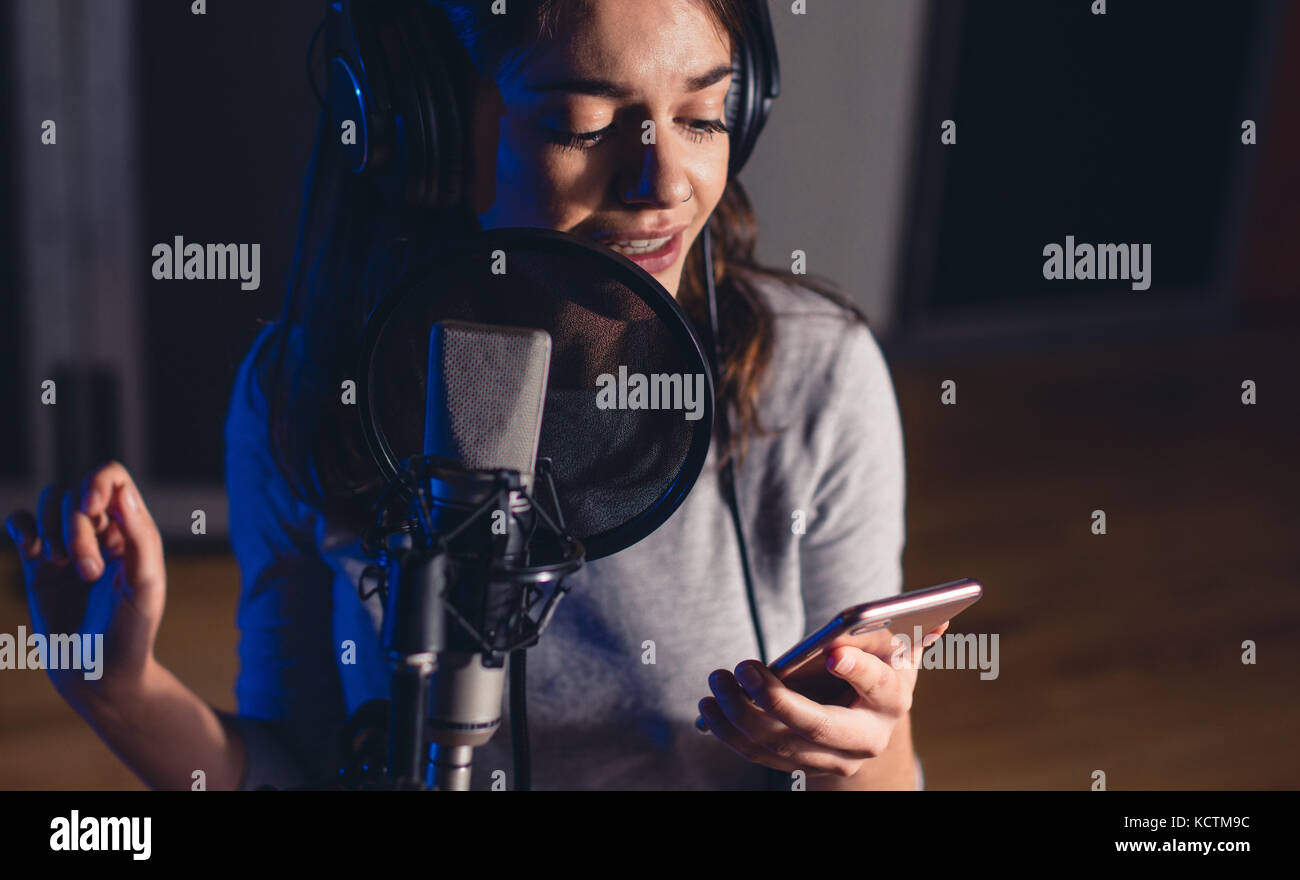 Young artist singing a song in the recording studio with mobile phone ...