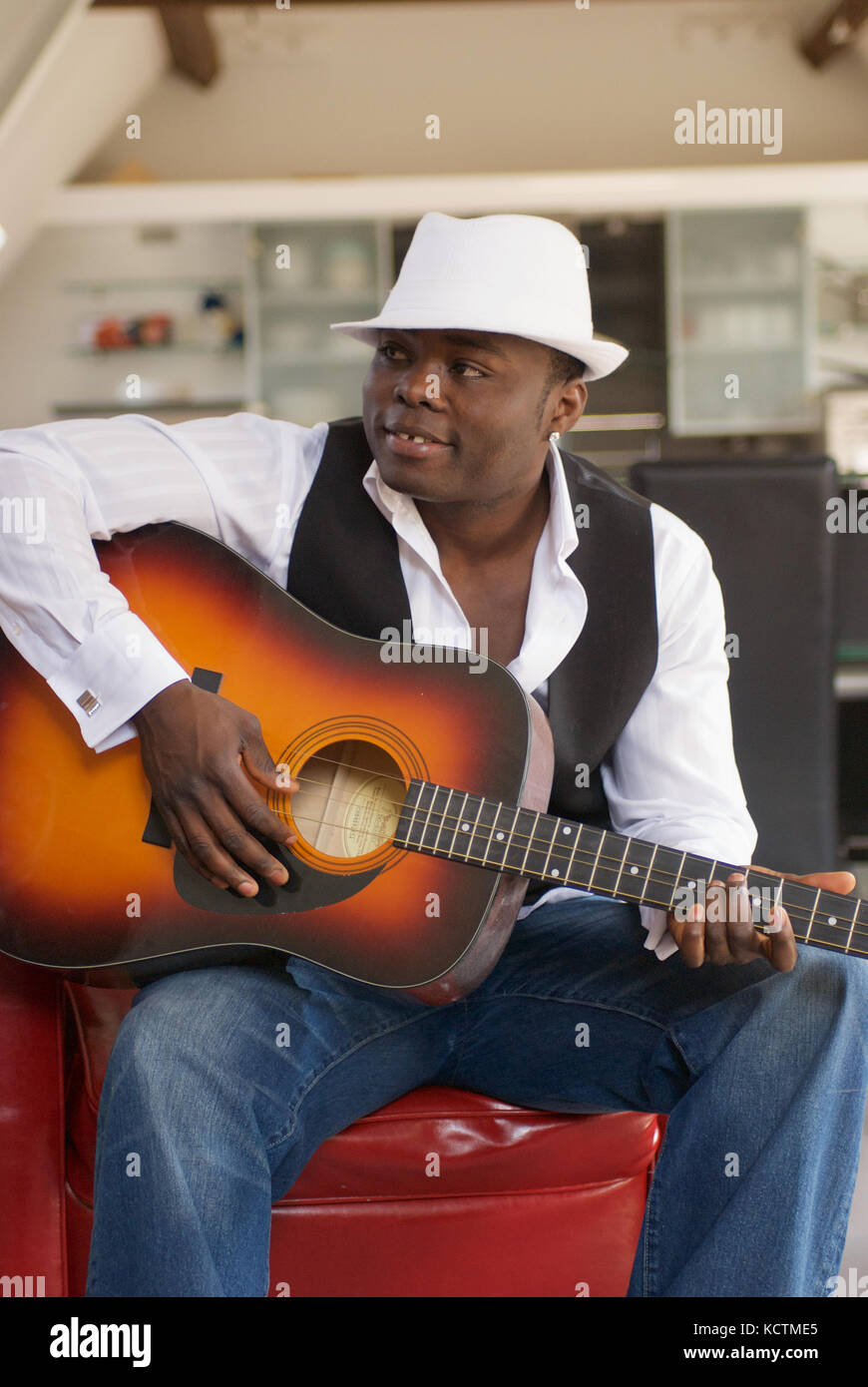 A young man sitting with a guitar in a lounge Stock Photo - Alamy