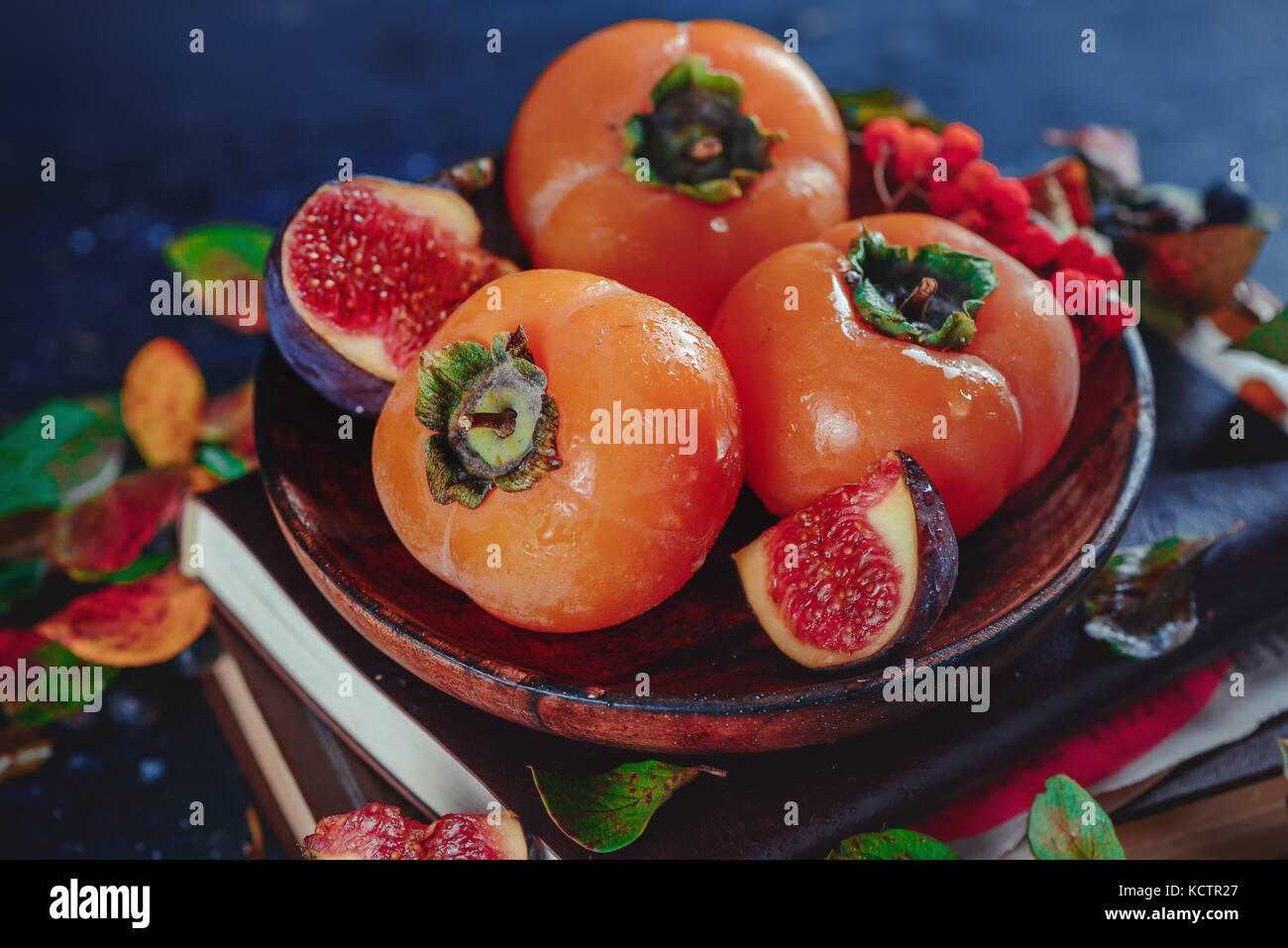 Ripe persimmons on wooden plate in a dark autumn still life with fruits ...