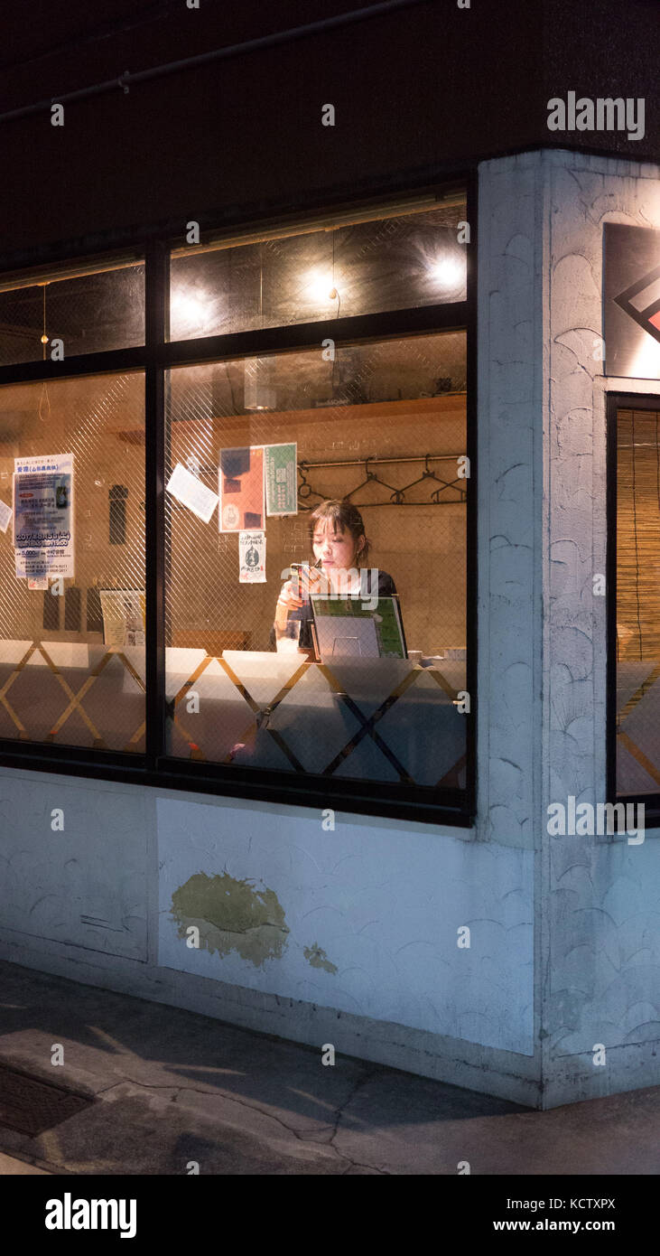 Young woman sitting at coffee shop window counter looking at her cell ...