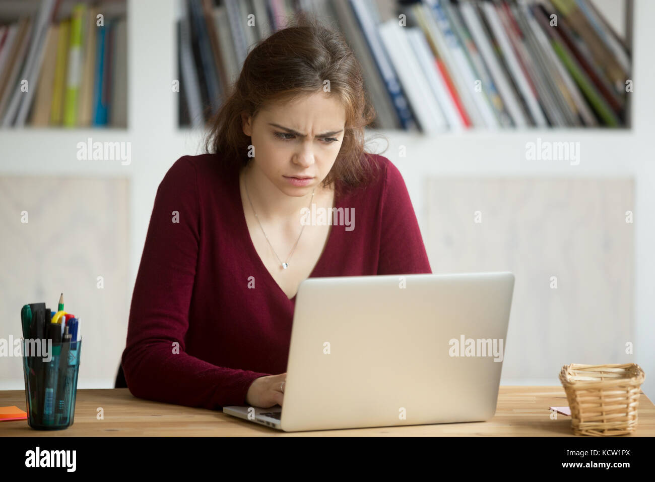Perplexed young casual female entrepreneur looking at laptop screen ...