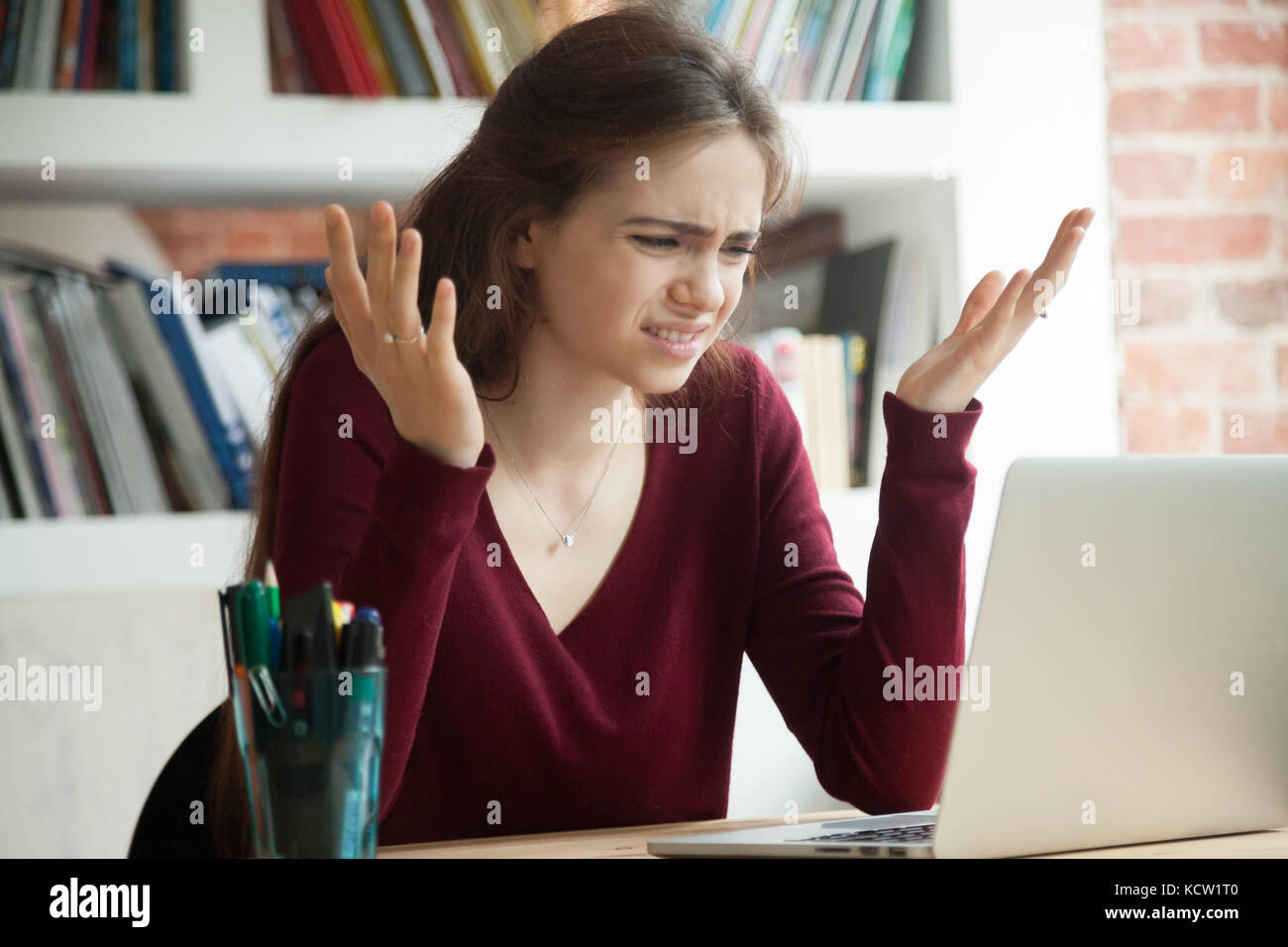 Perplexed female office worker shrugging while looking at laptop screen ...