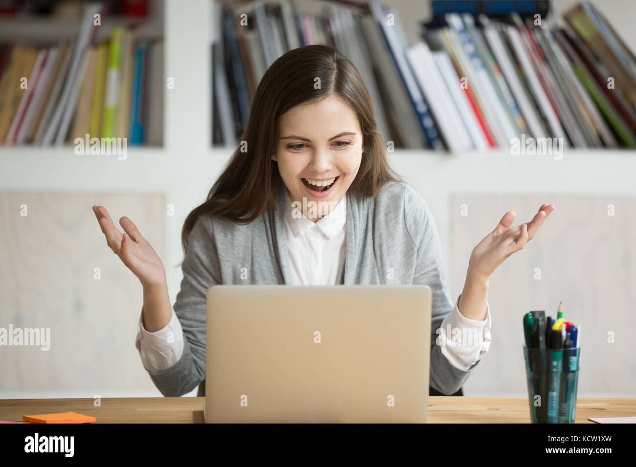 Young businesswoman looks at laptop screen with expression of joy and ...
