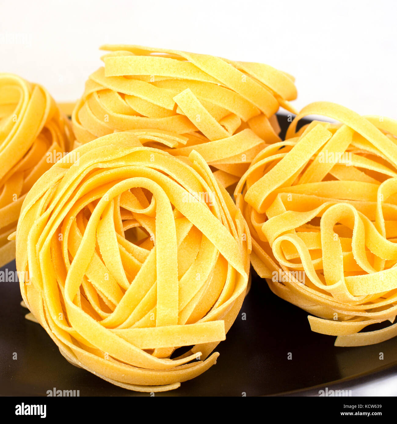 Uncooked tagliatelle on black ceramic plate. Isolated Stock Photo - Alamy