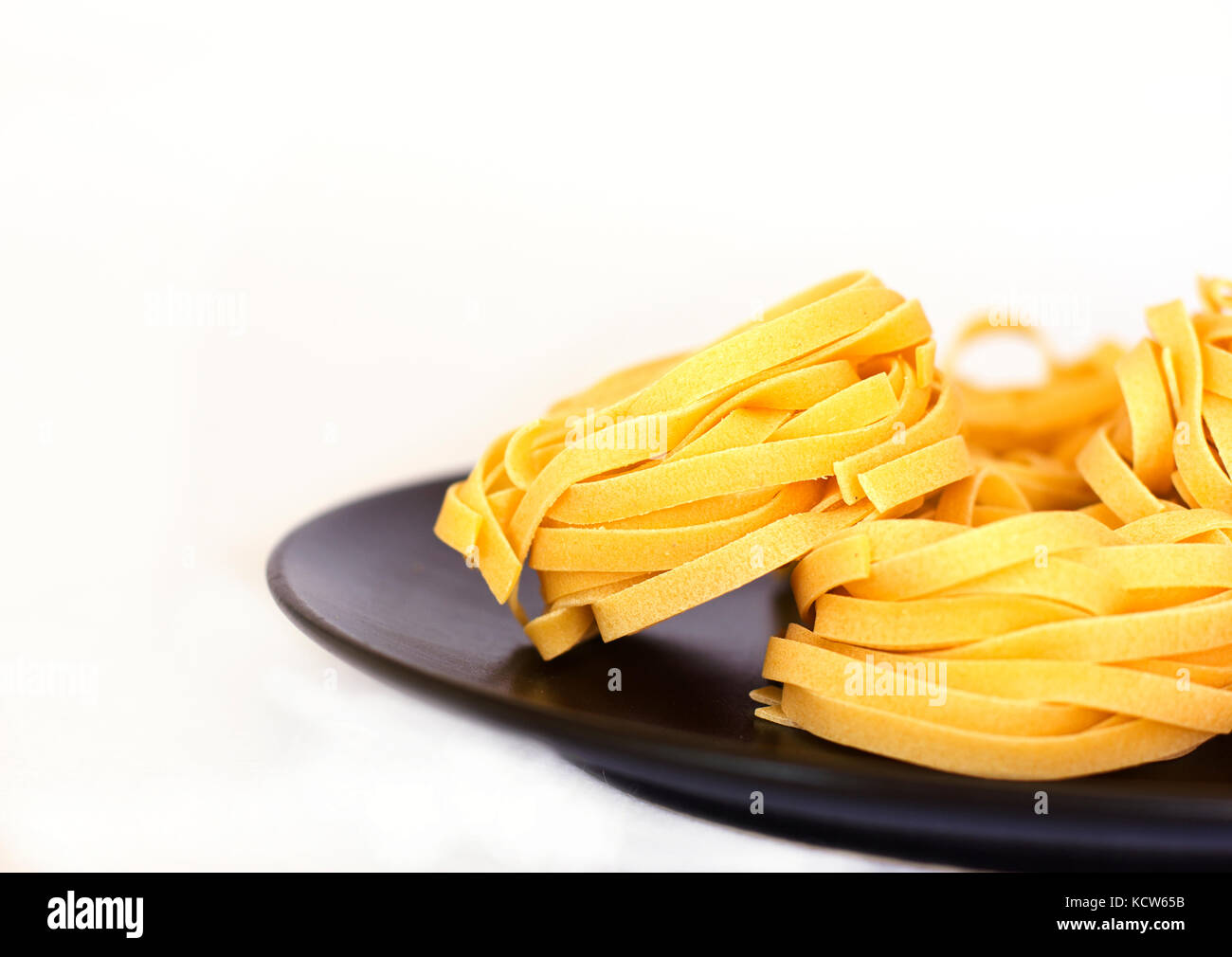 Uncooked tagliatelle on black ceramic plate. Isolated Stock Photo - Alamy