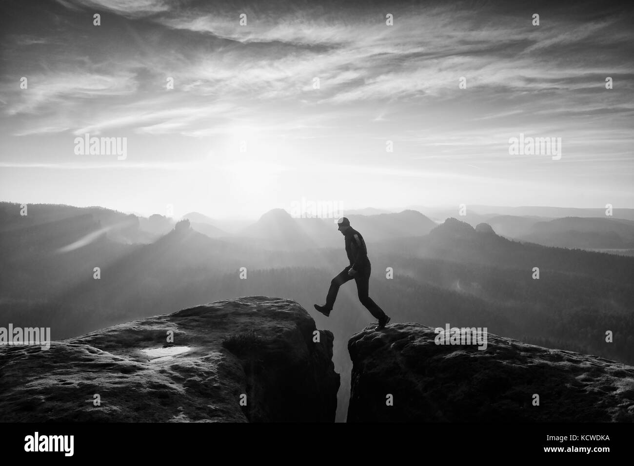 Crazy hiker in black is jumping between rocky peaks. Happy man ...