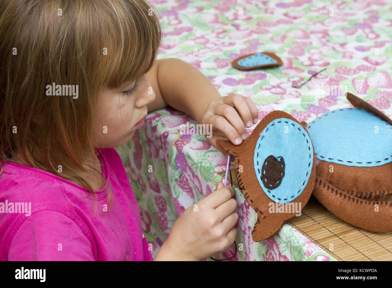 Cute creative little girl sewing a dress for her teddy bear doll ...