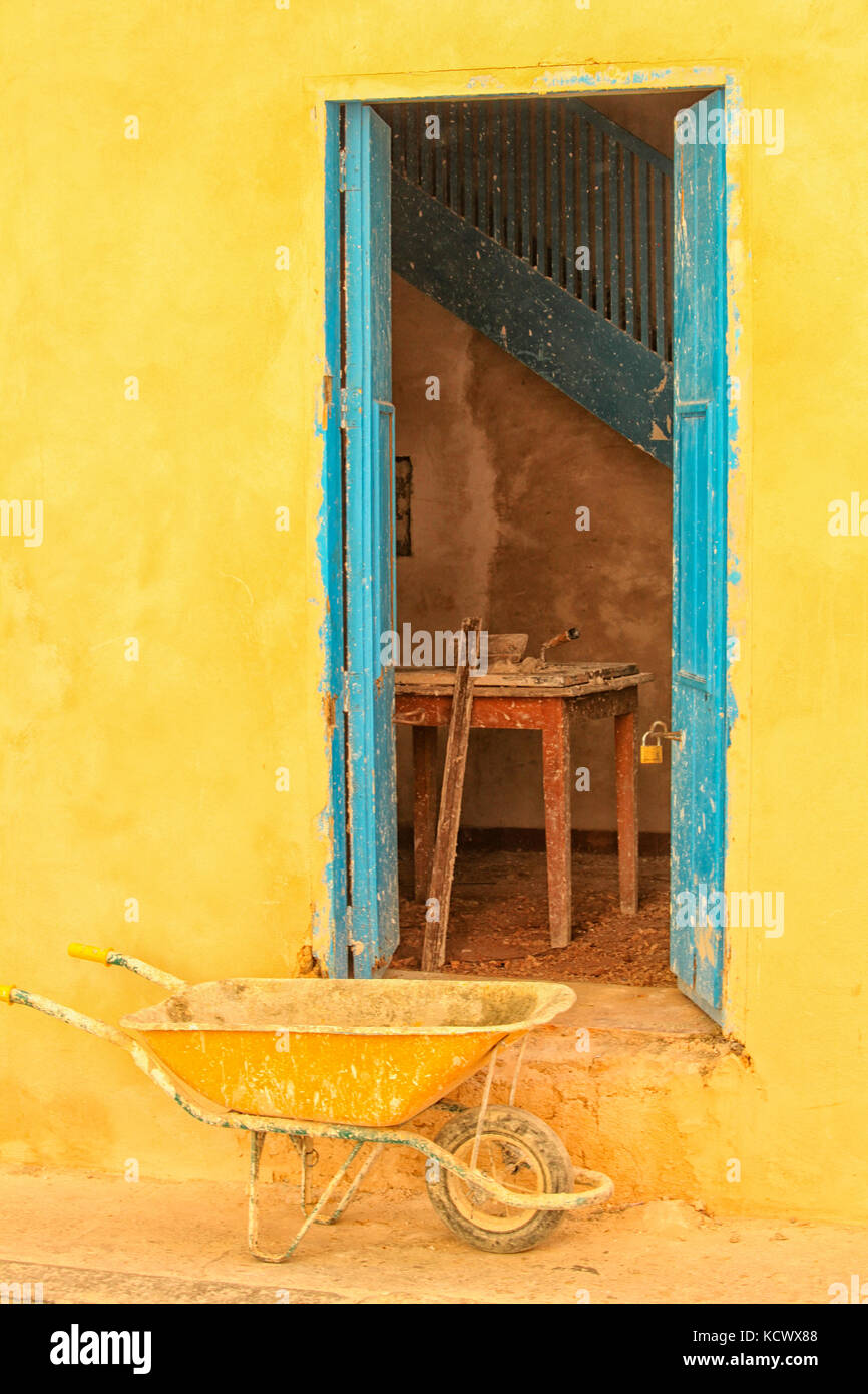 Yellow wheelbarrow in front of yellow wall and open wooden door painted ...
