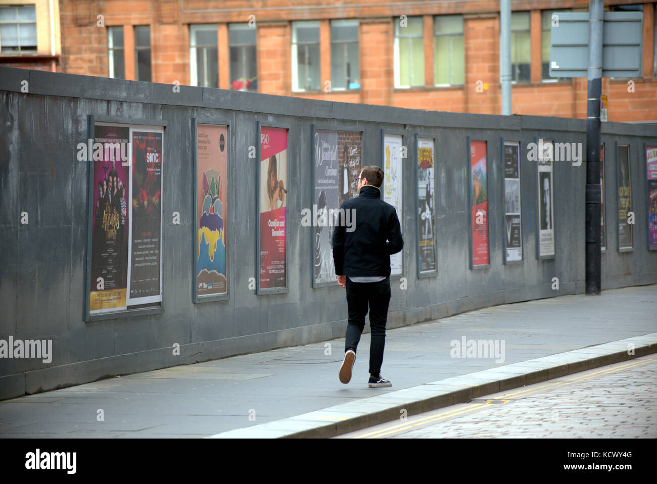 young man looking at fly posters on the street from pavement viewed ...