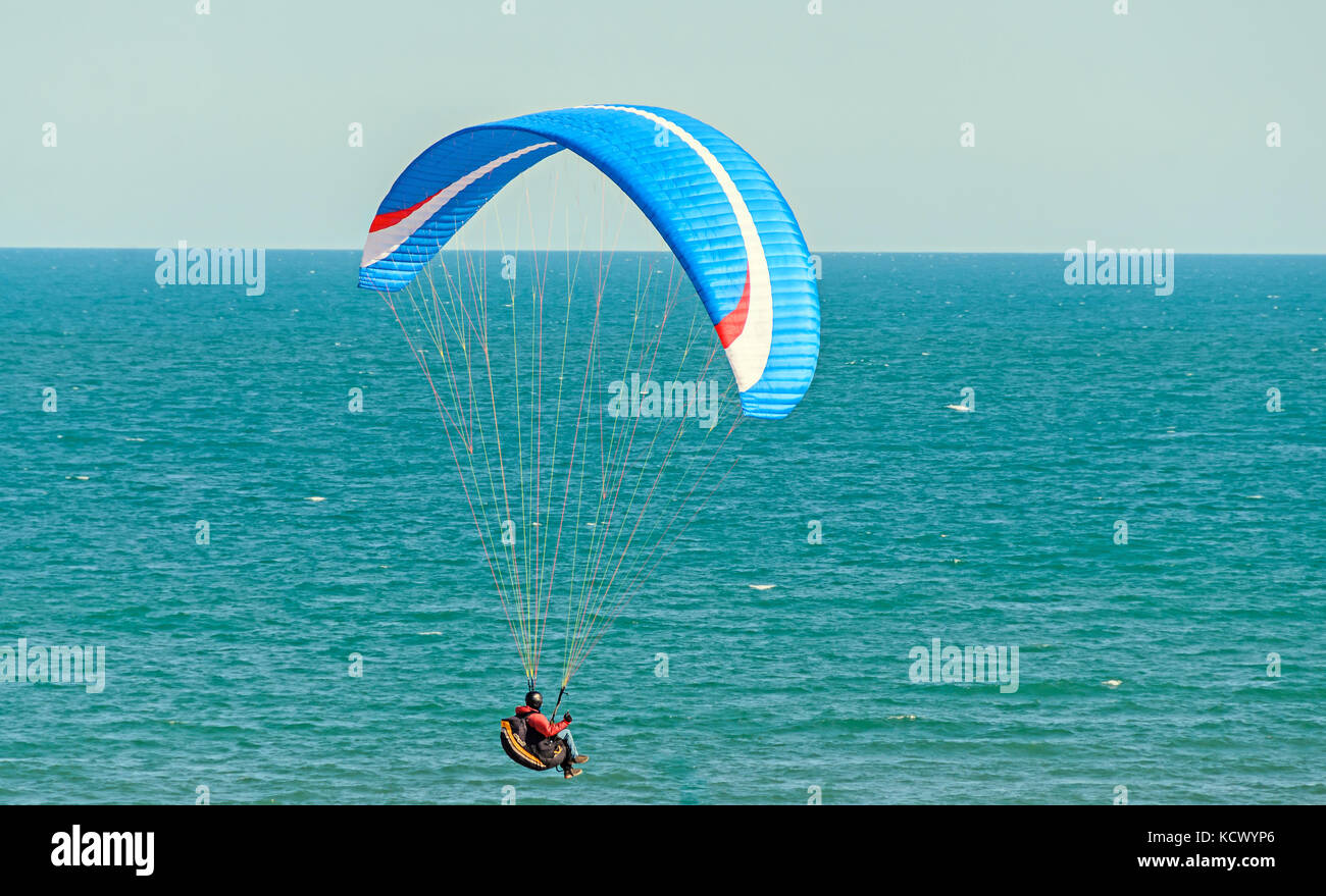 Man paragliding with blue parachute above water sea, clear sky Stock ...