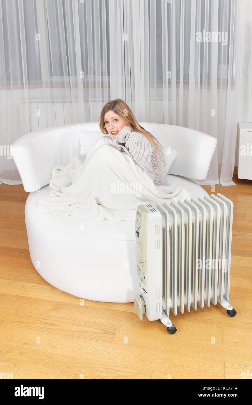 Young girl trying to keep warm at home next to electronic radiator and ...