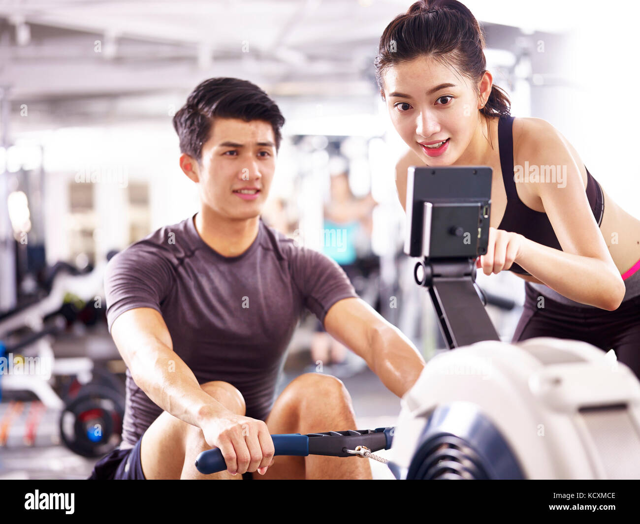 young asian man and woman working out in fitness center using rowing ...