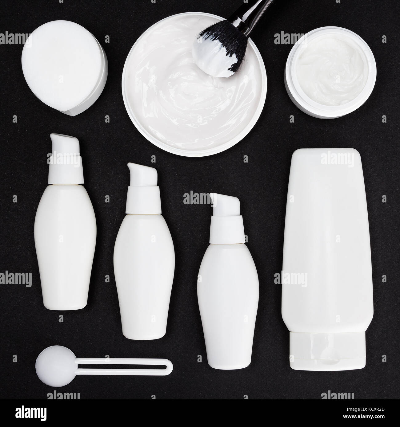 White cosmetic containers on black surface. Open jar of skin care cream ...