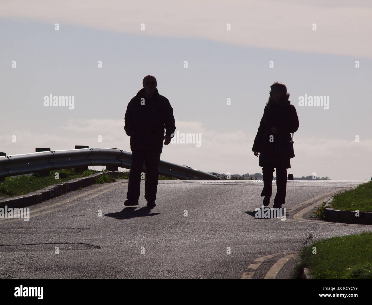 People strolling over the rise of a hill silhouetted by a high sun on ...