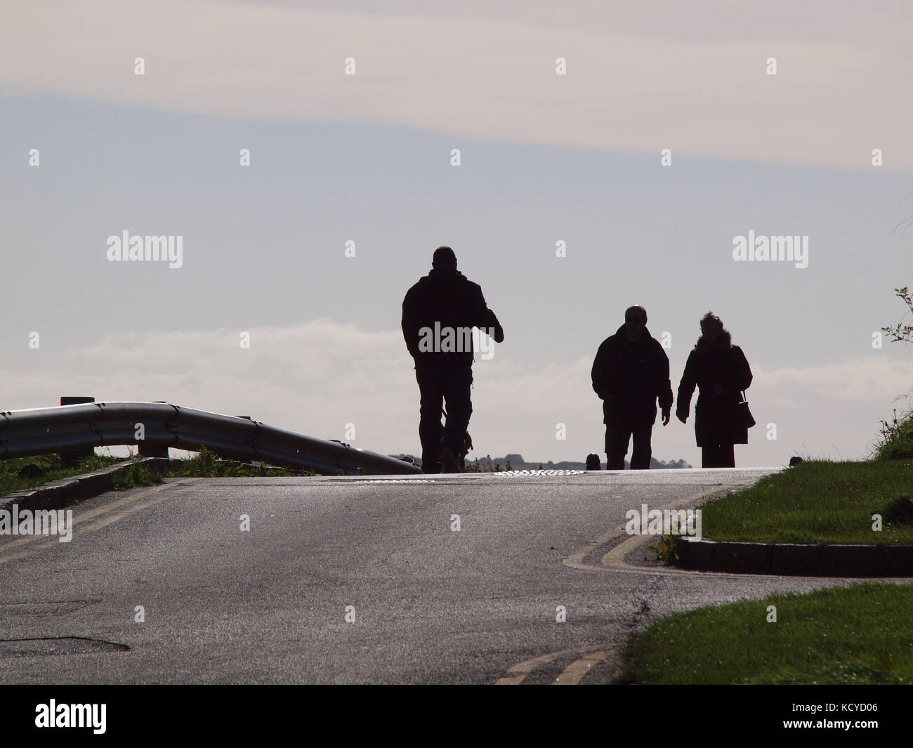 People strolling over the rise of a hill silhouetted by a high sun on ...