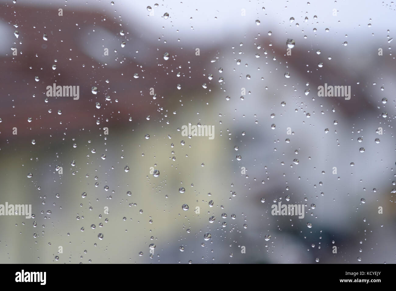 Water drops from rain at the glass of a window with blurred houses ...