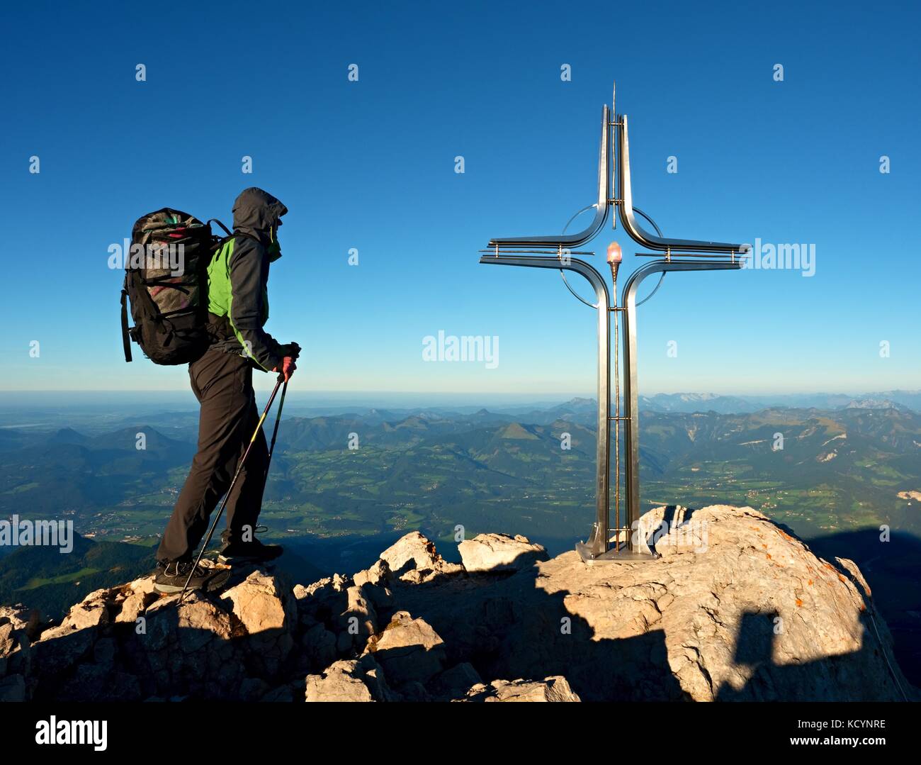 Hiker at big crucifix on mountain peak. Iron cross at Alps mountain top ...