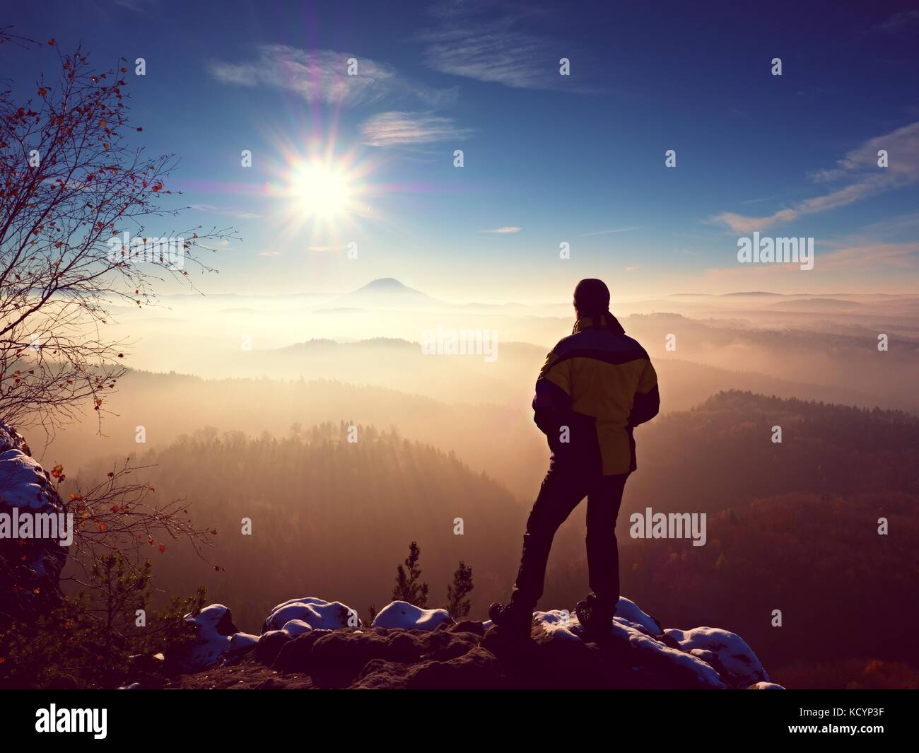 Tall hiker in black on rocky peak watch the world . Heavy orange mist ...