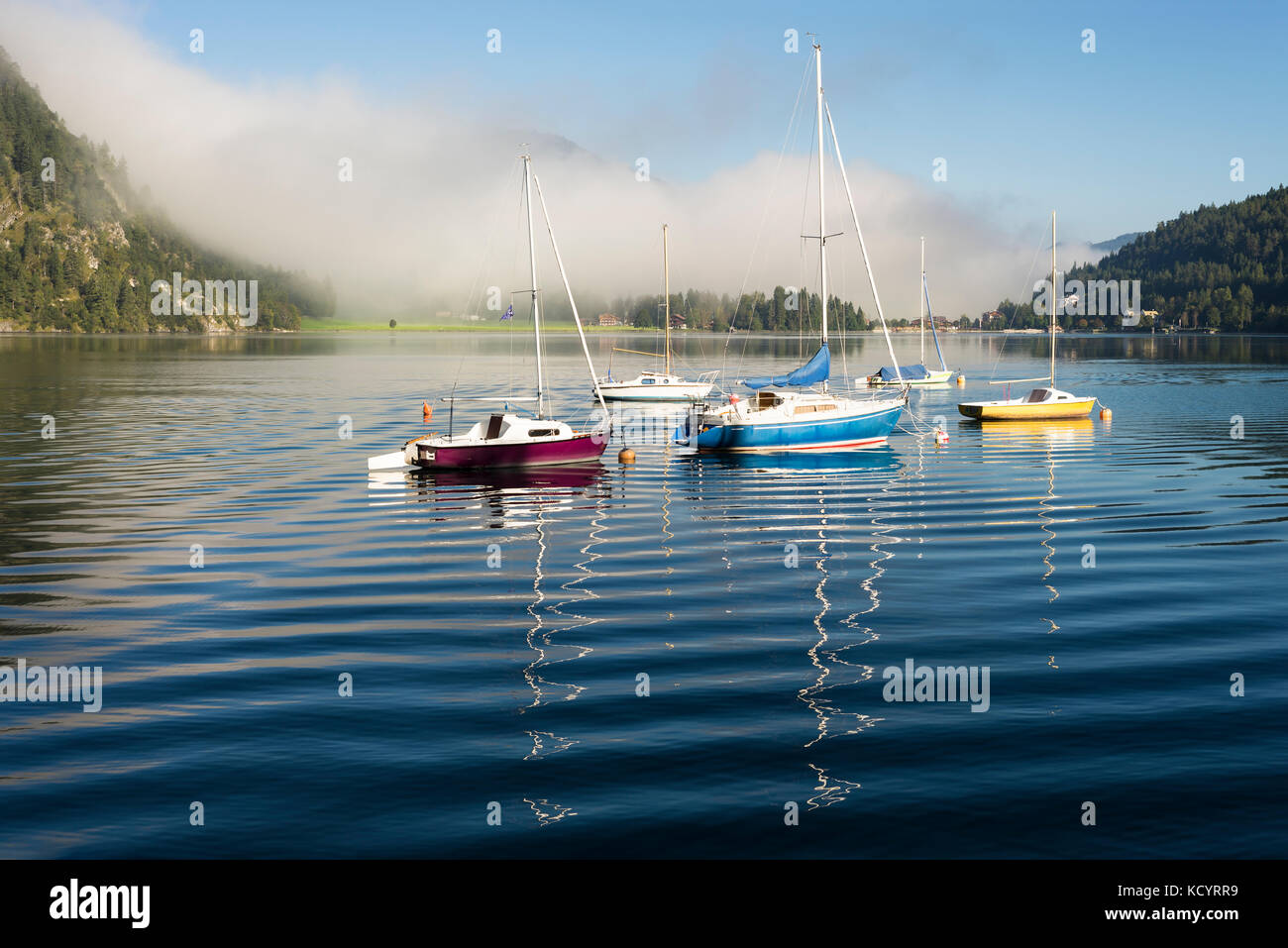 Mist, mountains, sailing boats and yachts in the morning sun reflected ...
