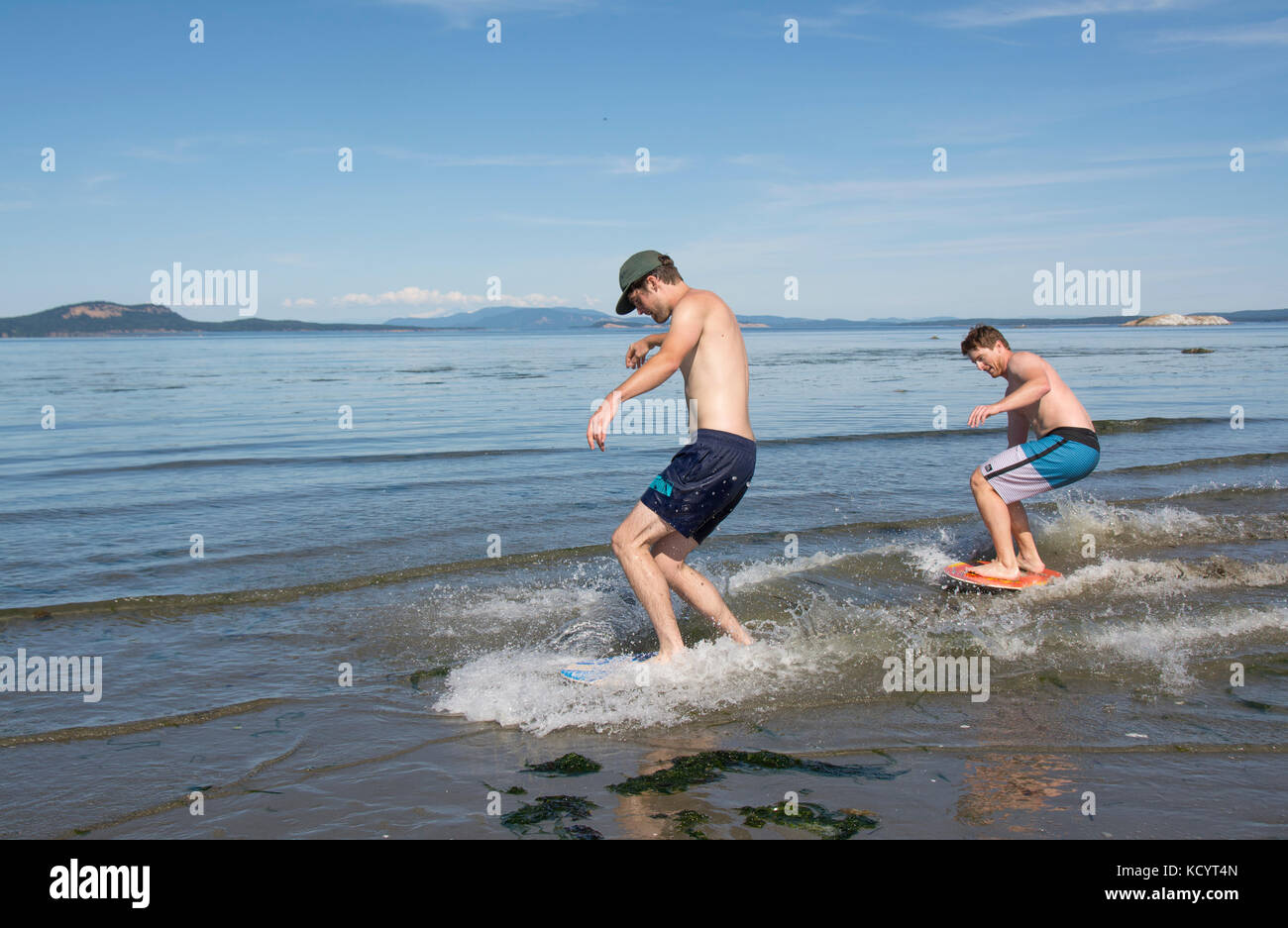 Young men skim boarding on the beach at Sidney Island, British Columbia ...