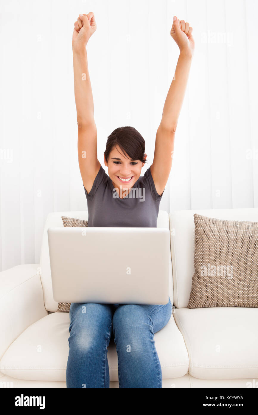 Excited Young Woman Sitting With Laptop On Couch Stock Photo - Alamy