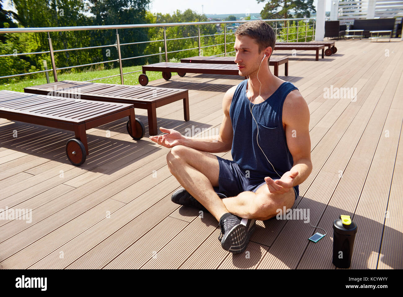Sporty young man sitting in lotus position and listening to music while ...