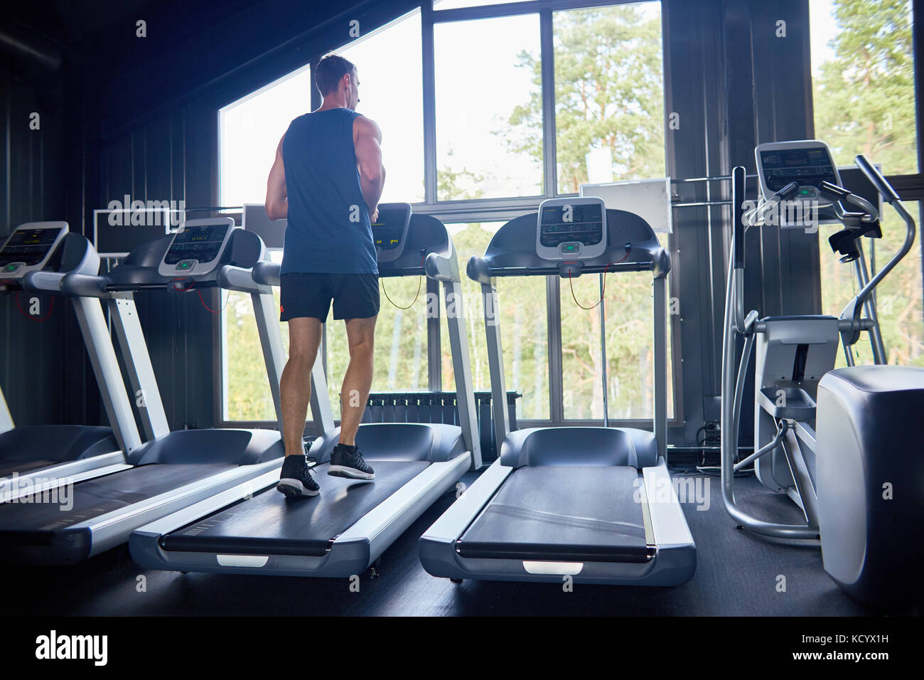Back view of muscular athlete doing exercise on treadmill and enjoying ...