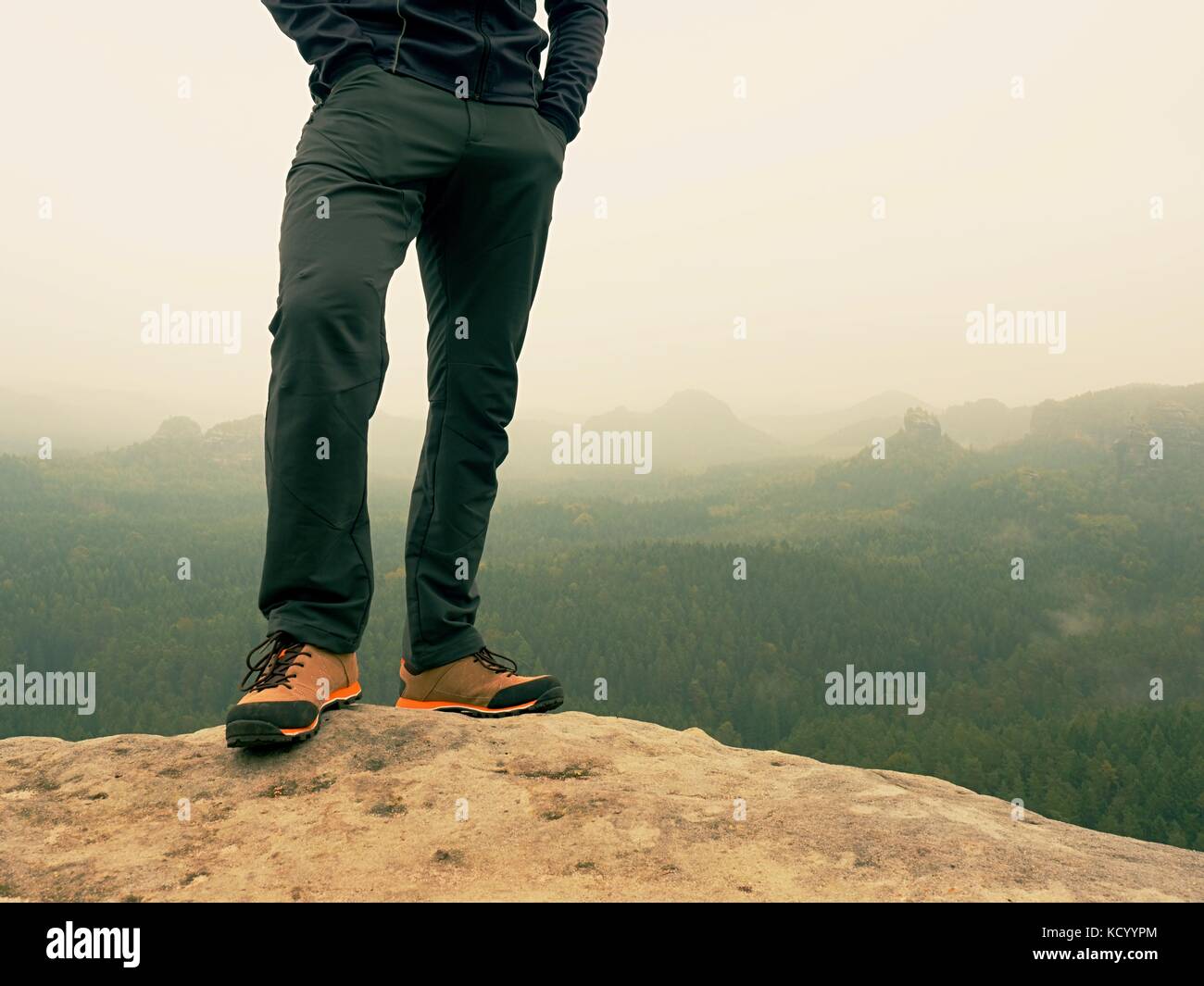Male legs in dark hiking trousers and leather trekking shoes on peak of ...