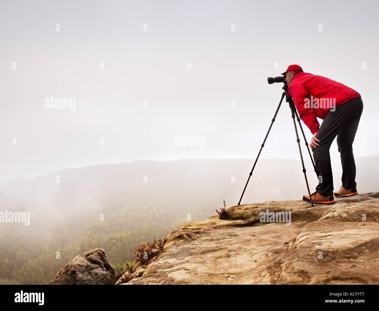 Hiker with camera on tripod takes picture from rocky summit. Alone ...